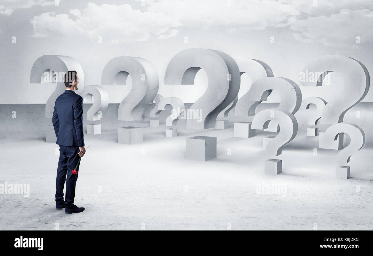 Businessman standing and looking to a bunch of question mark signs ...