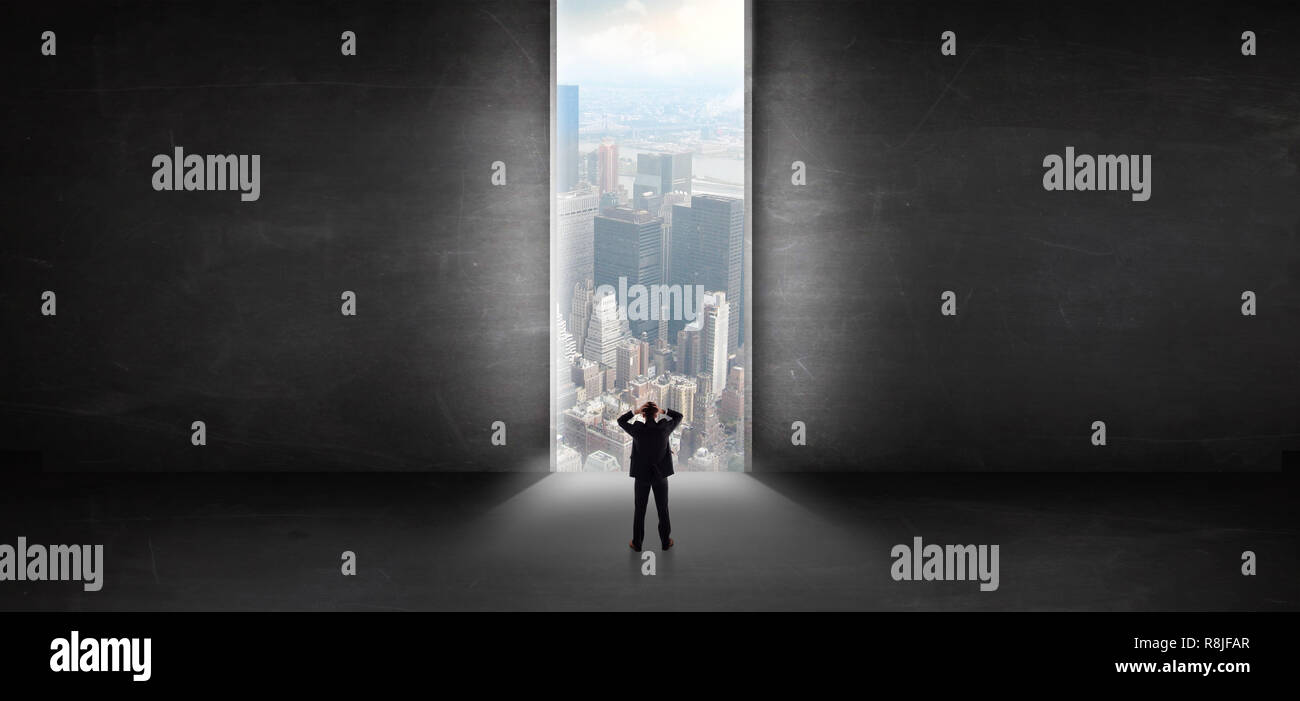 Businessman standing in a dark room and looking outside to a cityscape ...