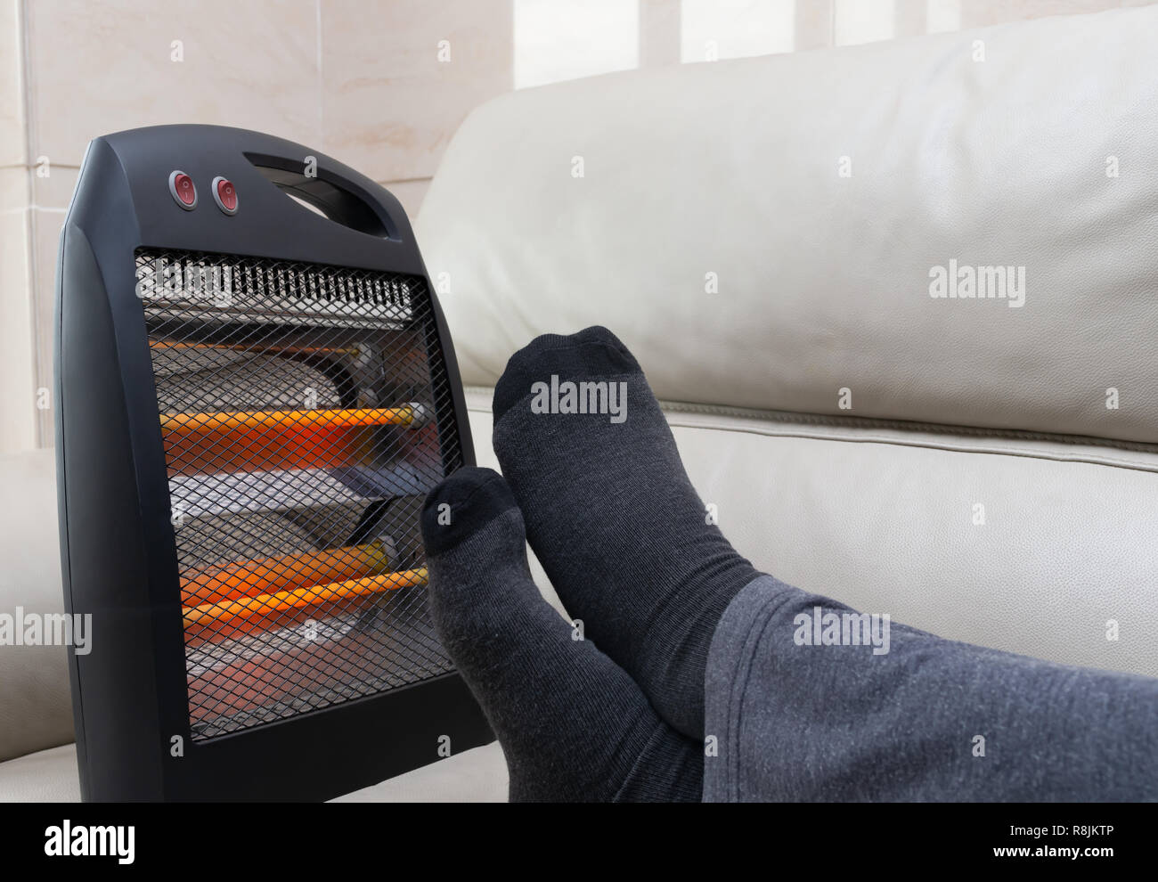 man lying on sofa with an electric heater near his feet Stock Photo - Alamy