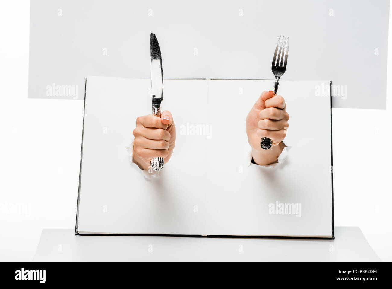 partial view of woman holding fork and knife through holes on white ...