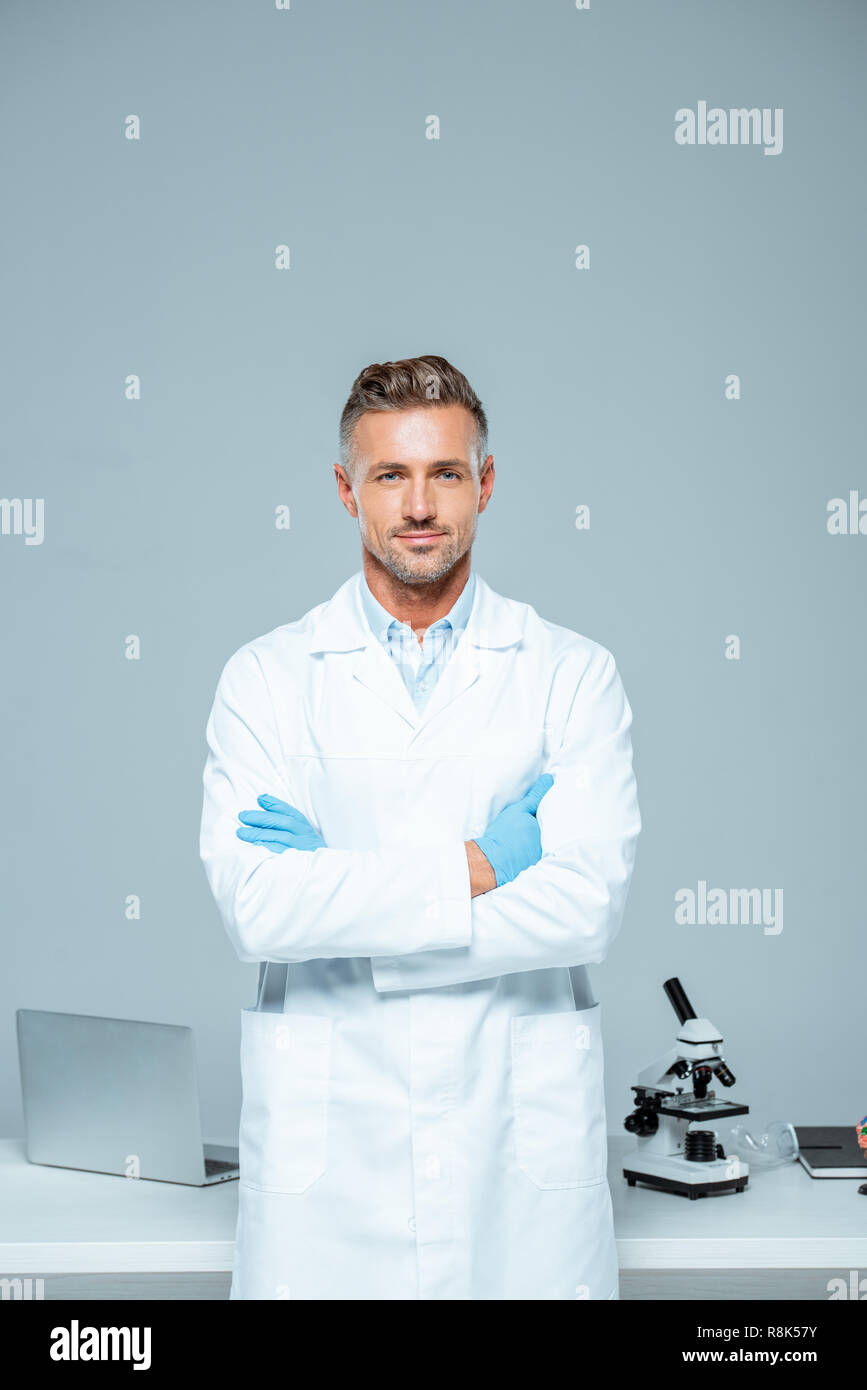 handsome scientist in white coat and latex gloves standing with crossed ...
