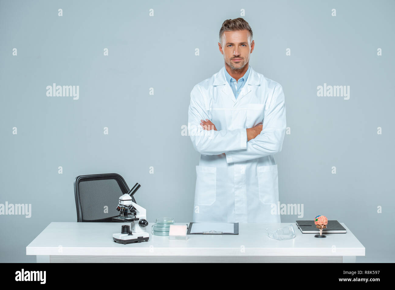 handsome scientist standing with crossed arms near table isolated on ...