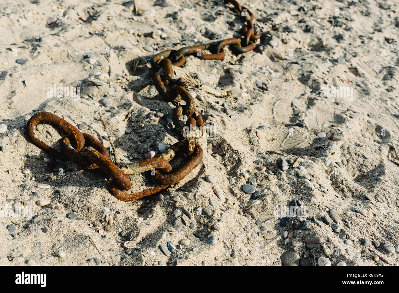 Concept of abandonment, old rusty and broken chains thrown in the sand ...