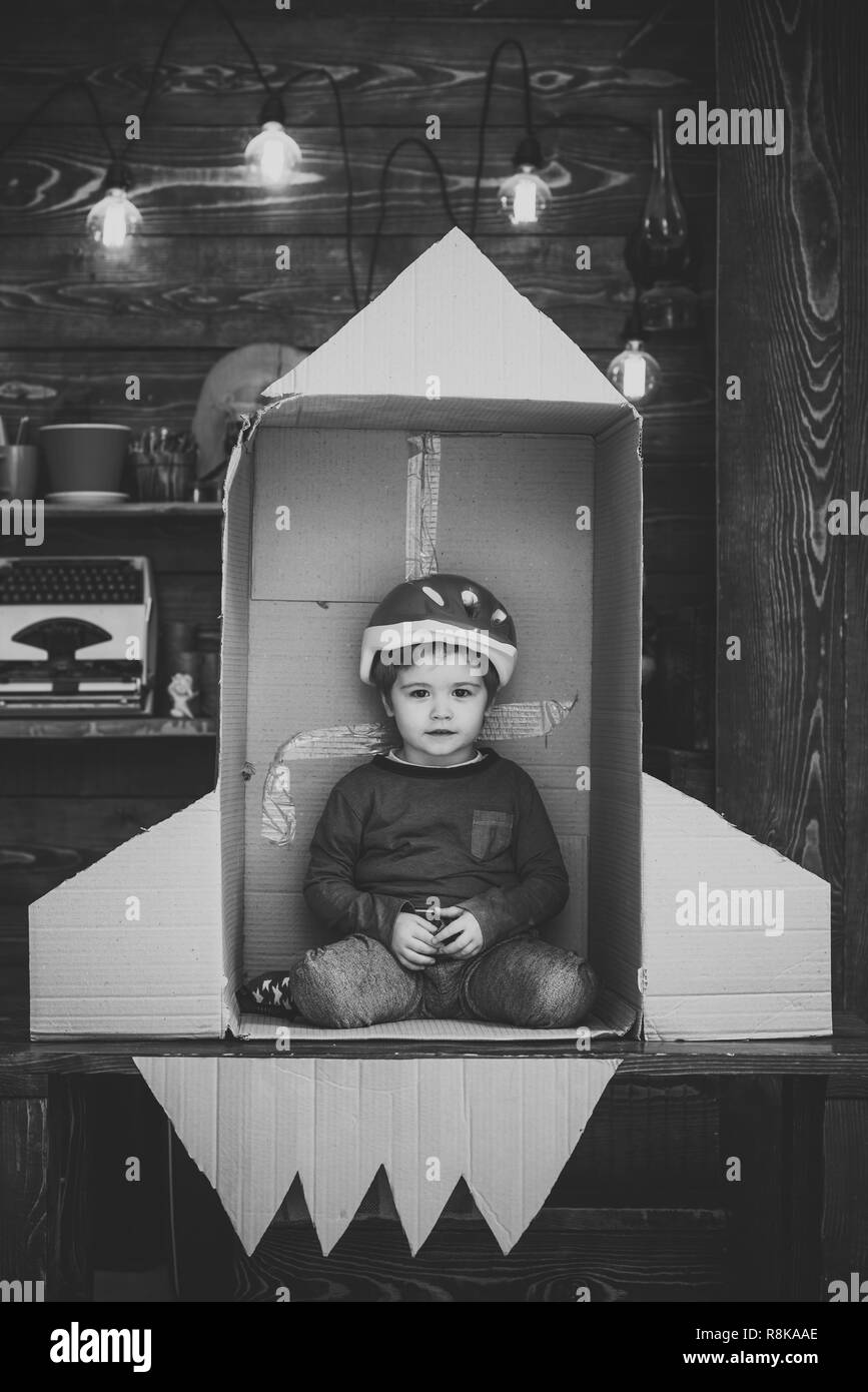 Kid in helmet sit in cardboard hand made rocket. Child boy play ...