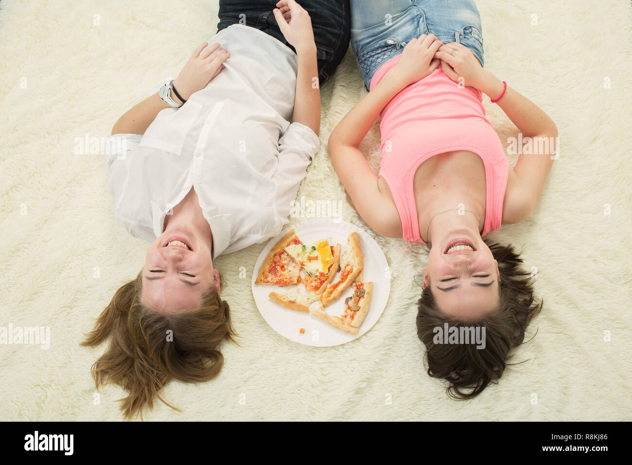 overeat happy girls lying on bed with pizza, laughing Stock Photo - Alamy