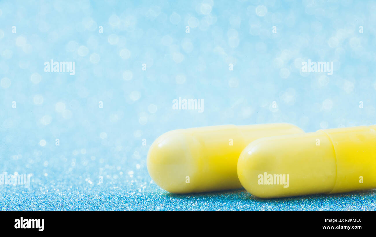 two yellow capsules closeup on blue glitter, sparkles, sparkling ...