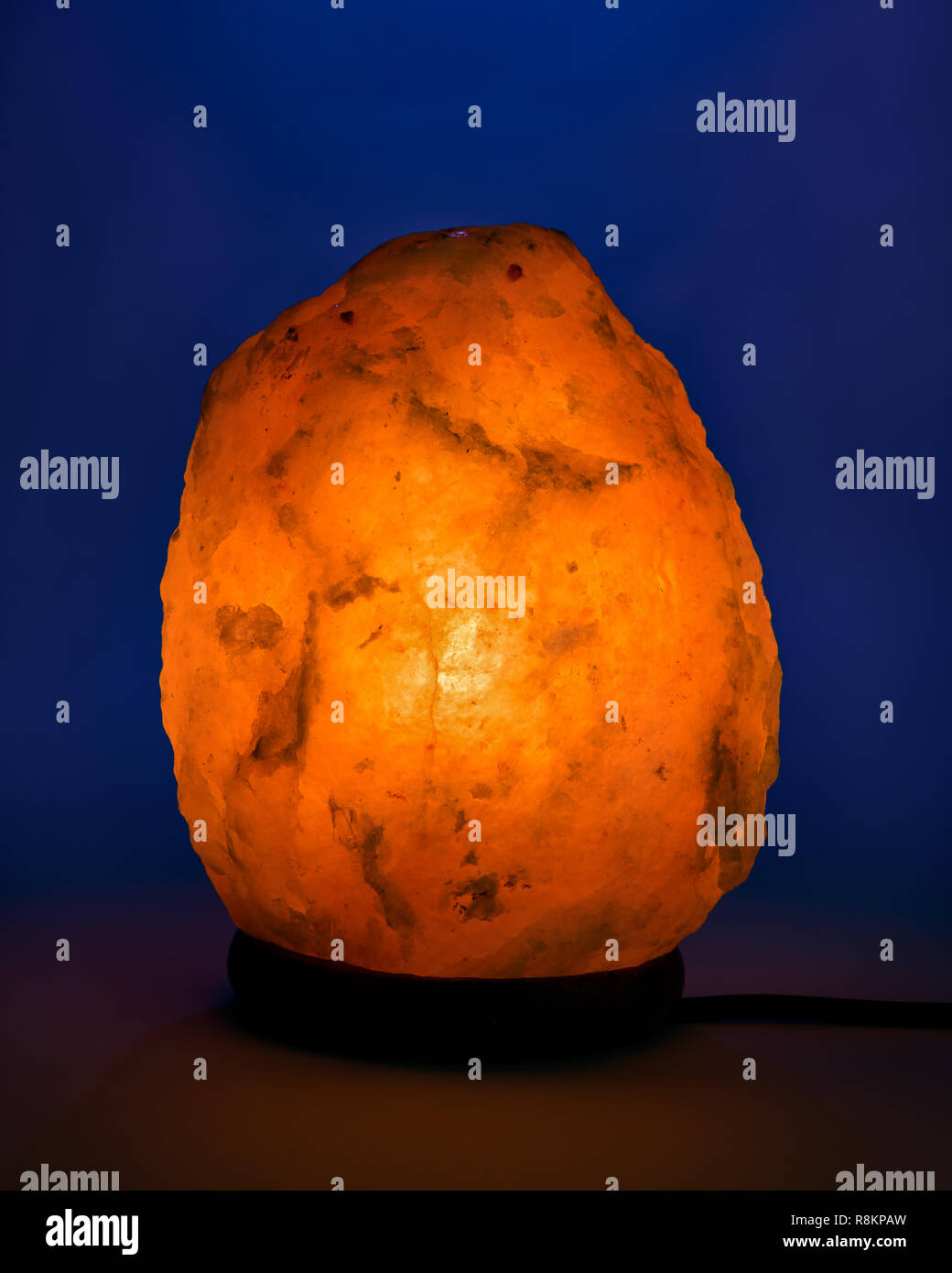 Small himalayan salt lamp glowing against plain blue background in dark ...
