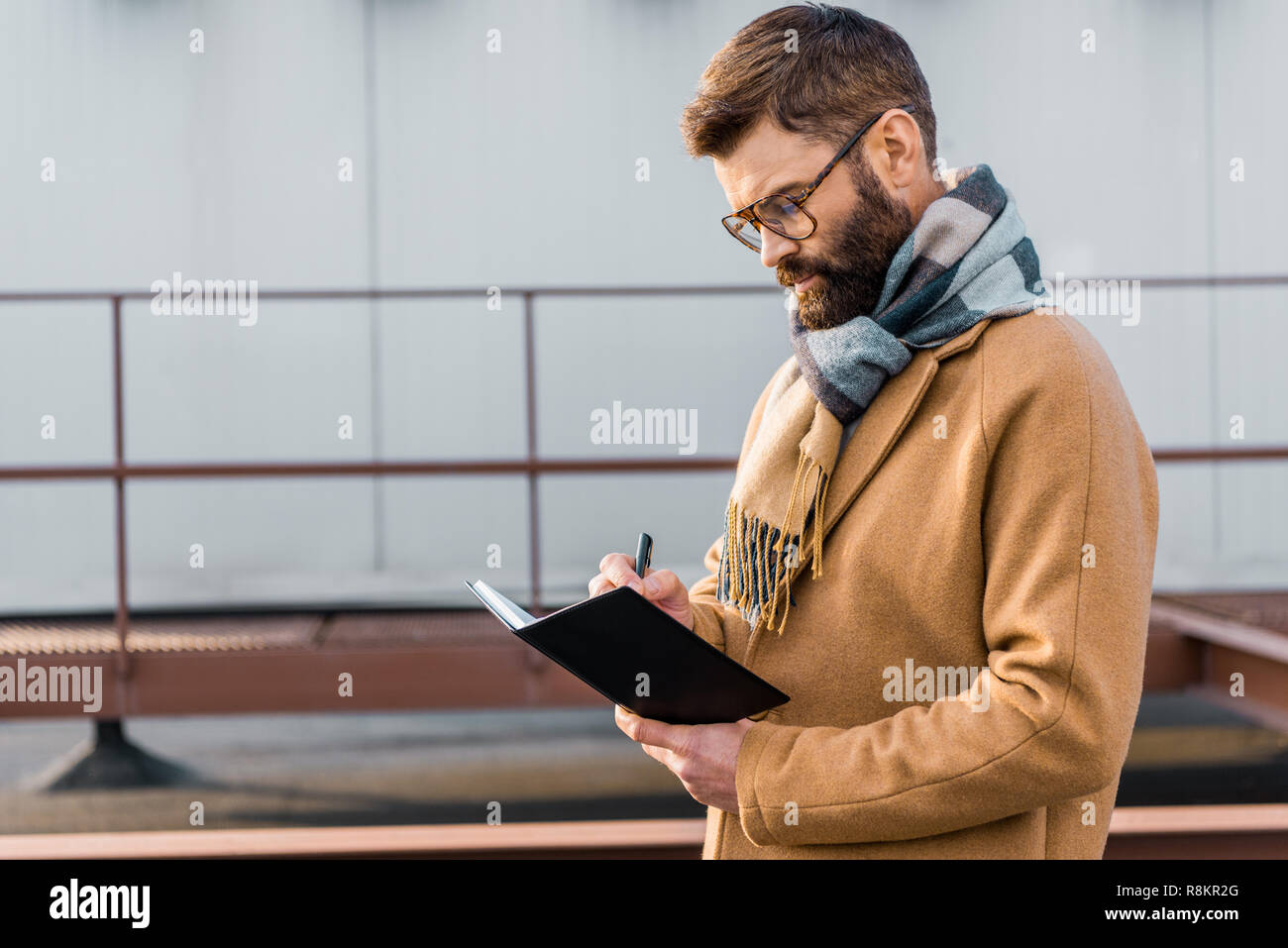 Focused businessman standing in coat and writing in notebook Stock ...