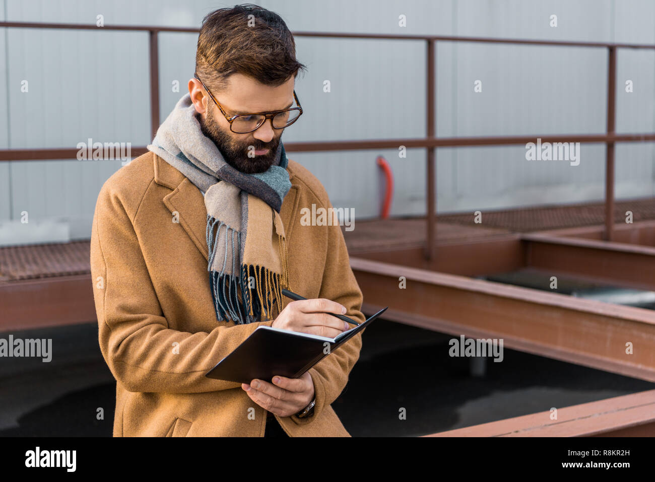 Bearded businessman standing in coat and writing in notebook Stock ...