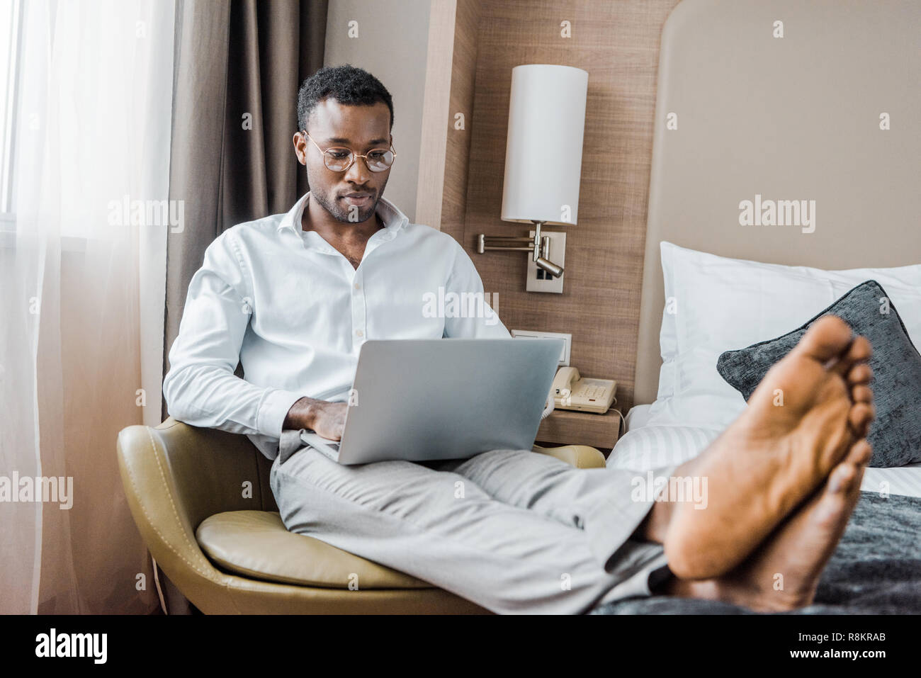 young barefoot african american businessman using laptop in hotel room ...