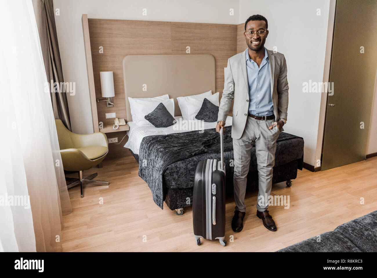 elegant african american businessman with suitcase in hotel room with ...