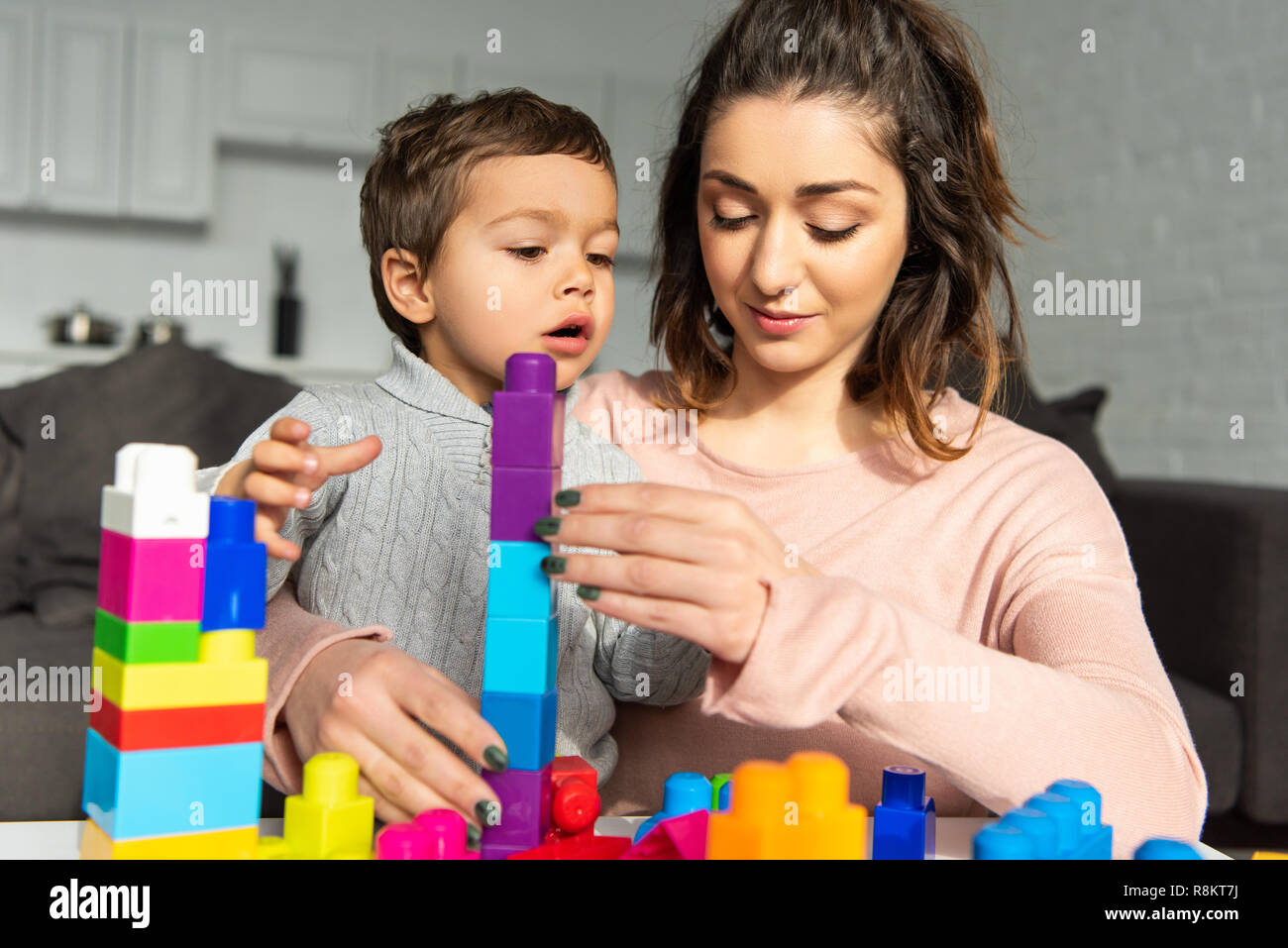 cute boy and his mother playing with colorful plastic blocks at home ...