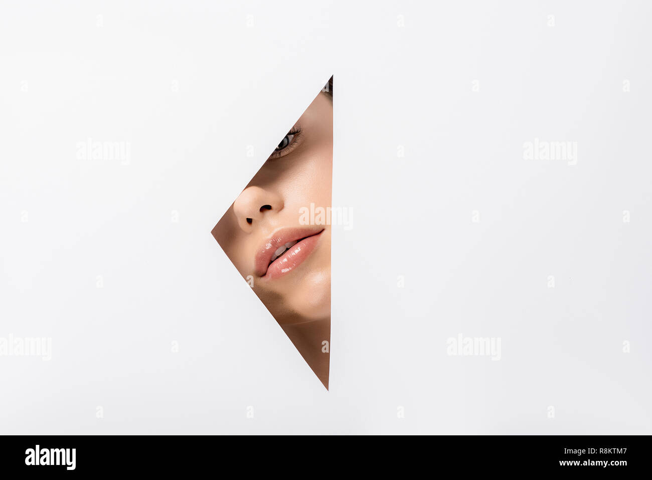 attractive young woman looking at camera through hole on white Stock ...