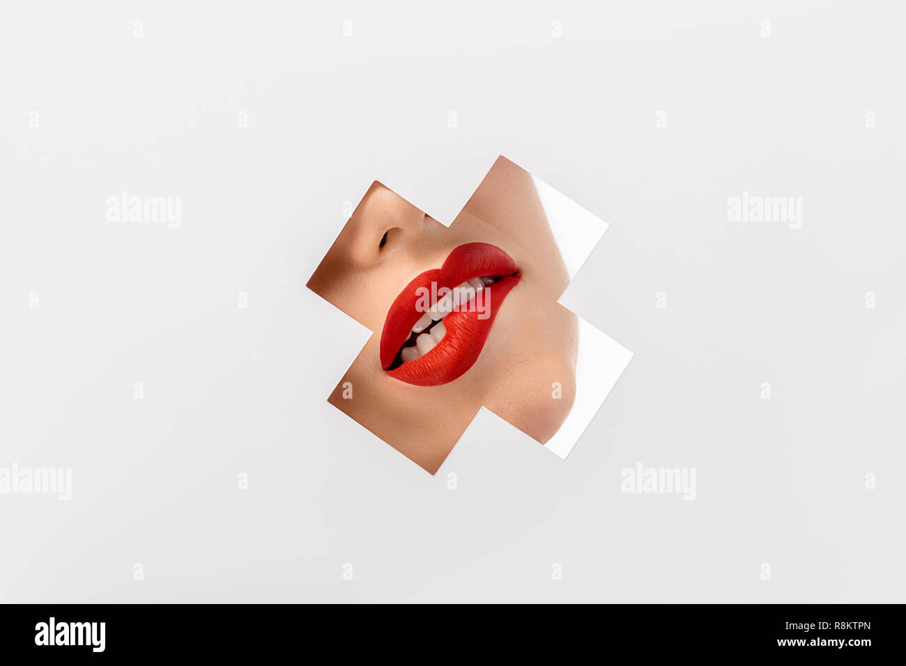 cropped shot of girl biting red lip through cross shaped hole on white ...
