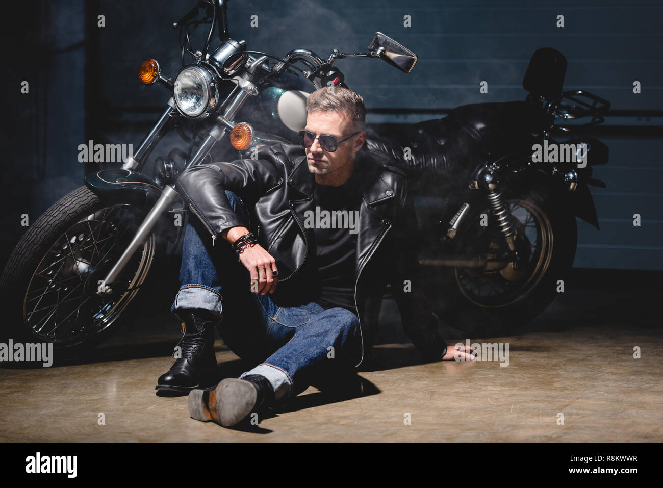 handsome biker in sunglasses sitting on floor next to motorcycle in ...