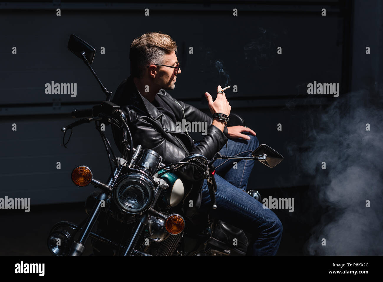 handsome biker in sunglasses sitting on motorbike in garage Stock Photo ...