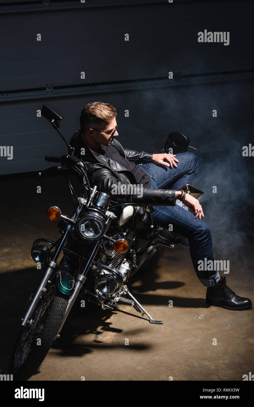 side view of handsome guy in sunglasses sitting on motorcycle in garage ...