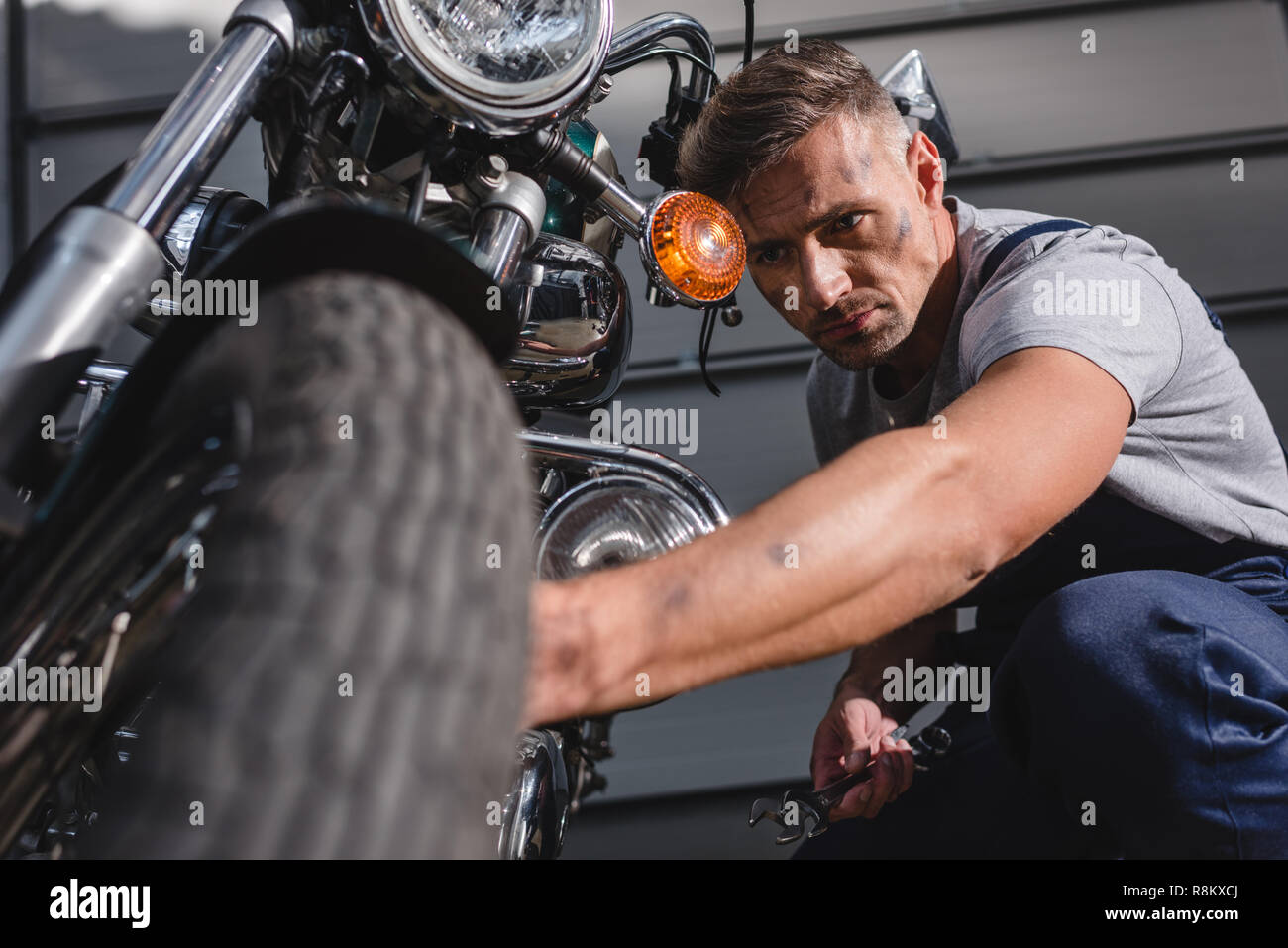 handsome adult mechanic fixing motorcycle tire in garage Stock Photo ...