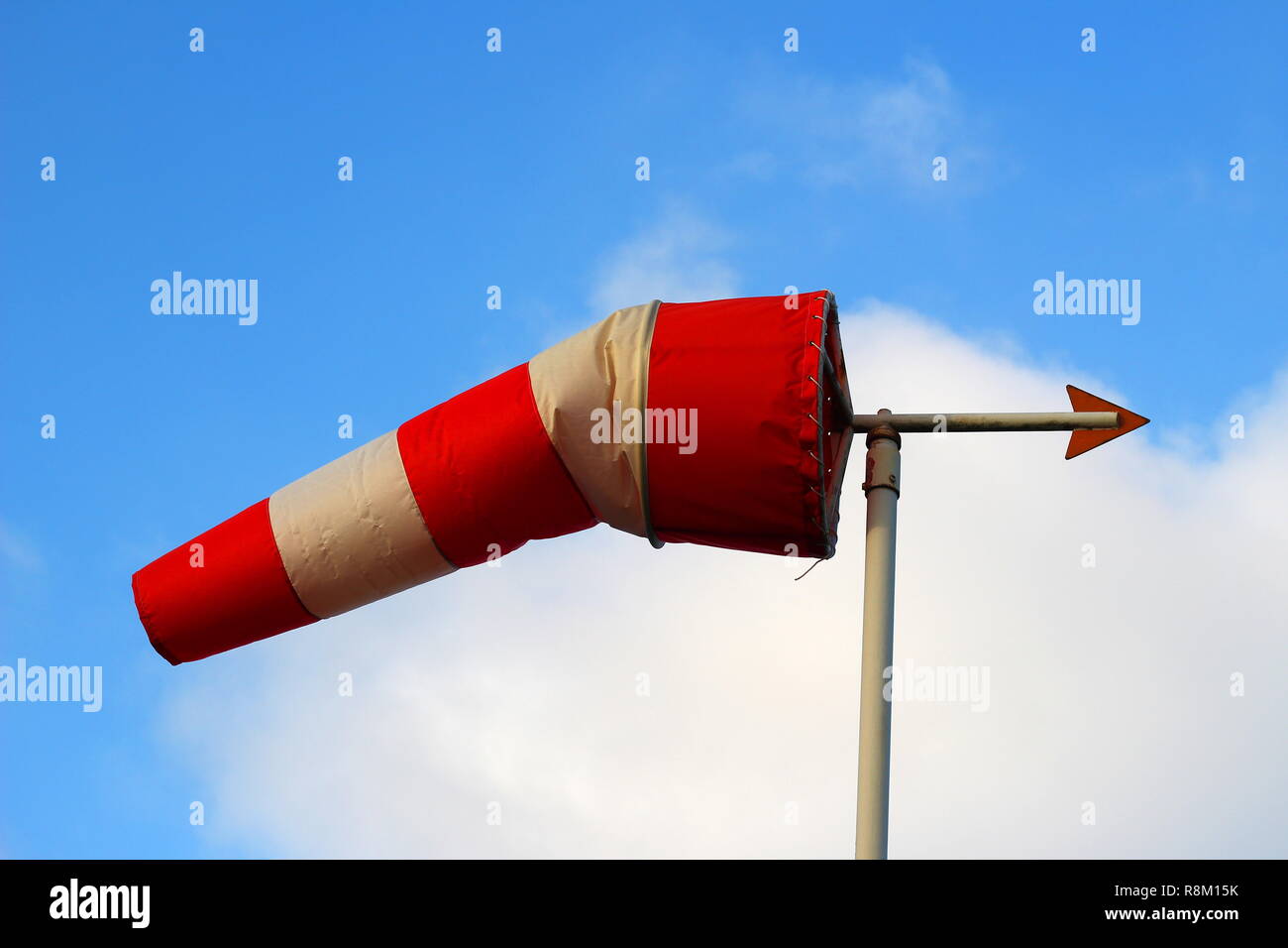A red and white windsock with a weather vane in front of a blue sky ...