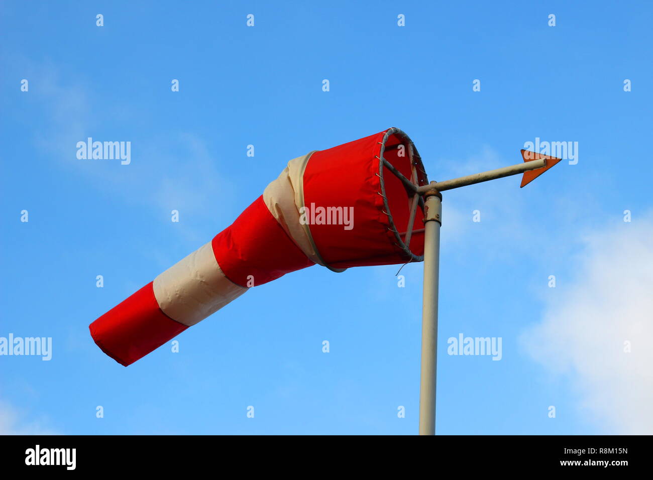 Windsock with a weather vane in front of a blue sky with wihite clouds ...