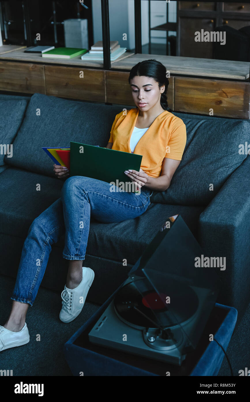 Beautiful Mixed Race Girl In Orange Shirt Choosing Vinyl On Sofa In