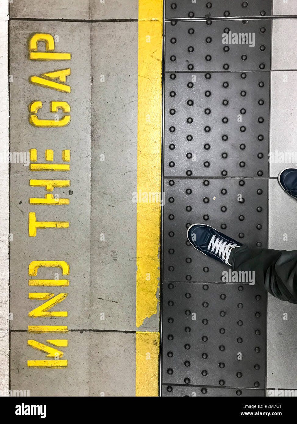 Feet stepping on ruber surface behind yellow safety line of London ...