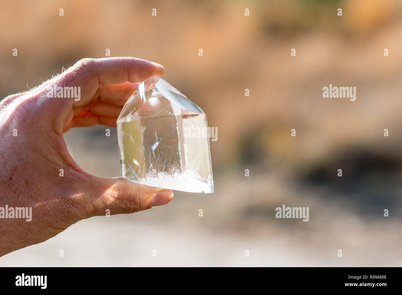 A Hand holding a transparent crystal quartz with the sun hitting the ...