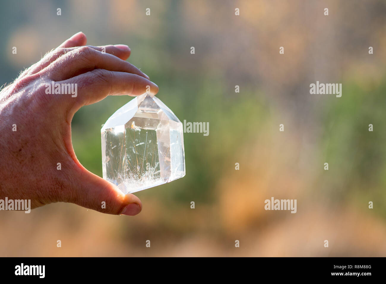 A Hand holding a transparent crystal quartz with the sun hitting the ...