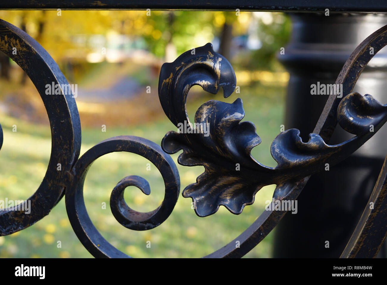 Forged fence close-up. Behind the fence is a park, a lamppost, a bridge ...