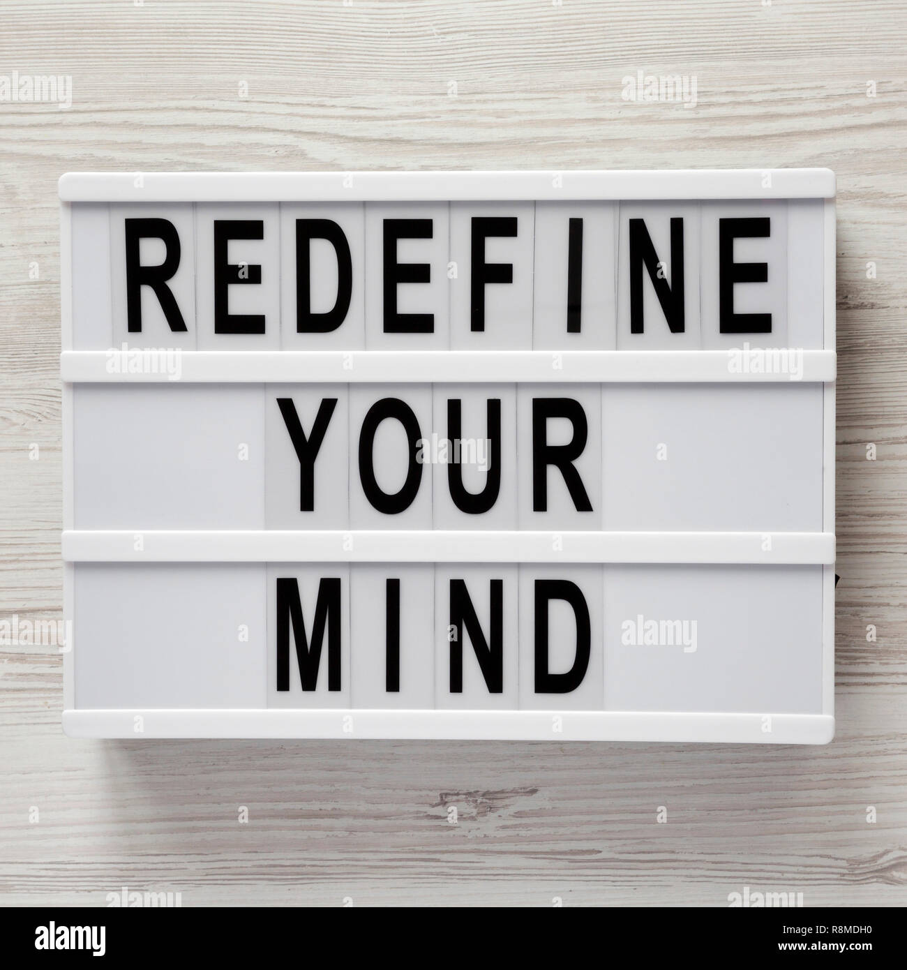 'Redefine your mind' words on modern board over white wooden background, top view. Overhead ...