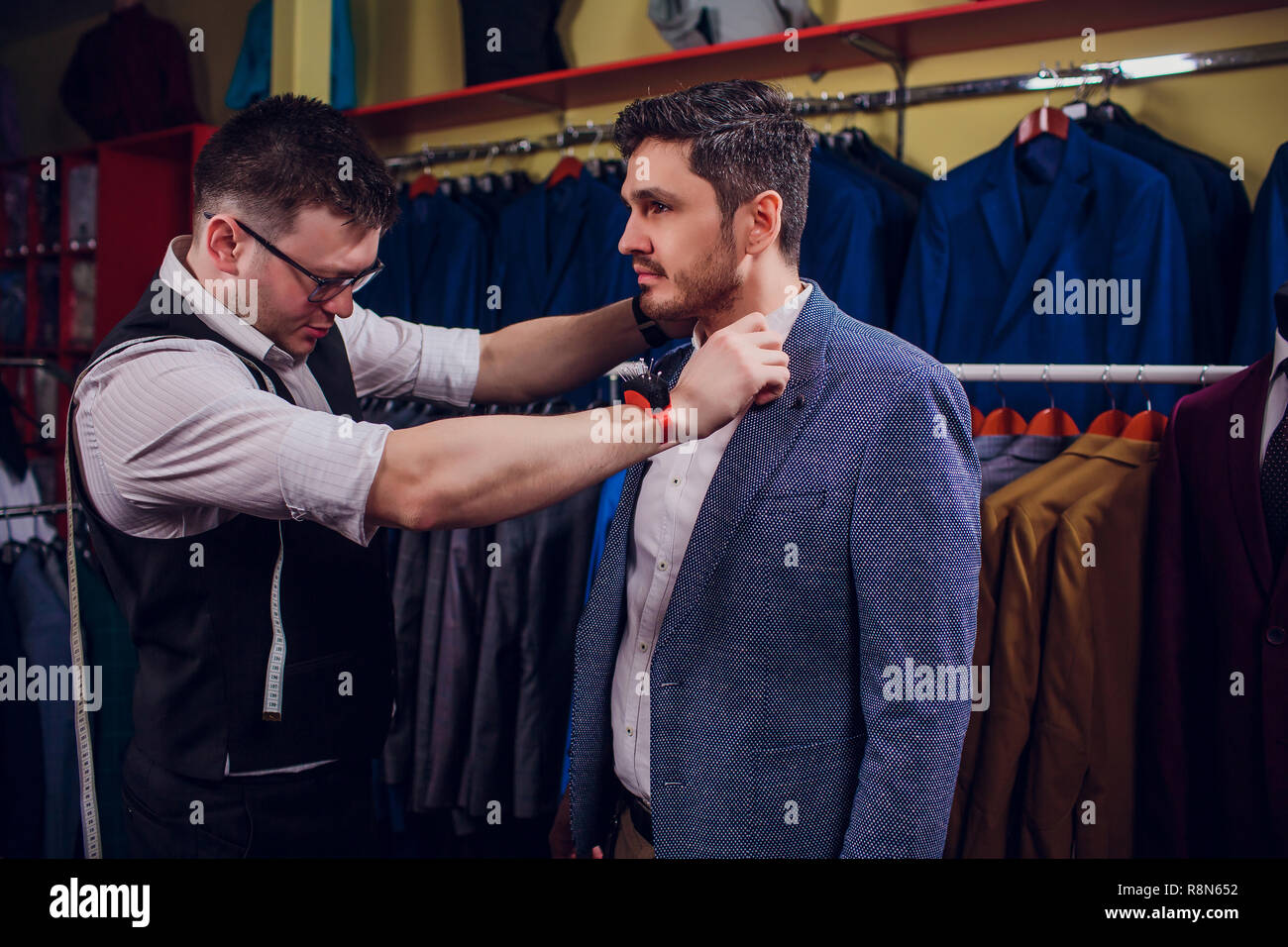 Businessman in classic vest against row suits in shop. Man helps ...