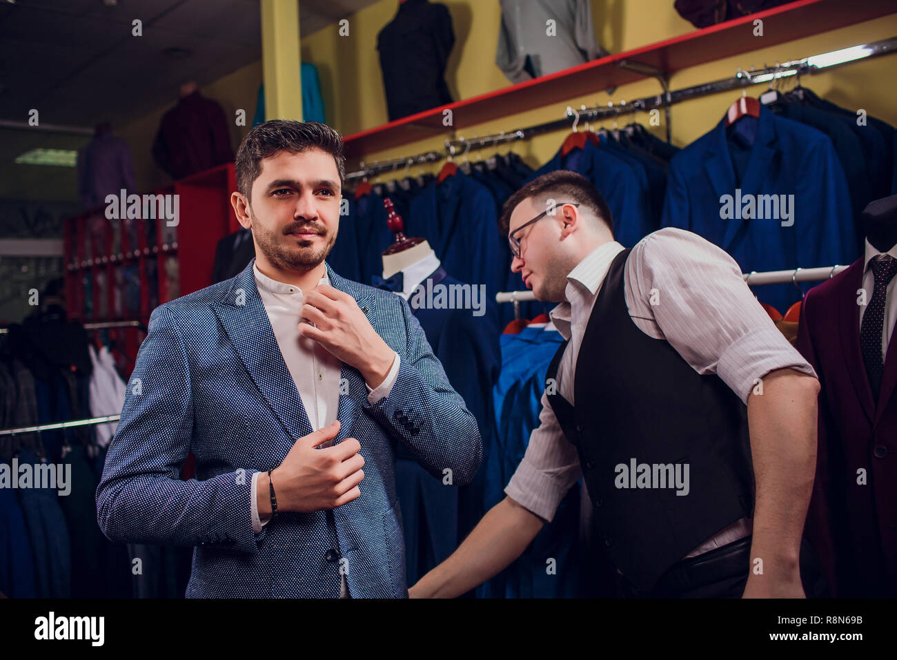 Businessman in classic vest against row suits in shop. Man helps ...