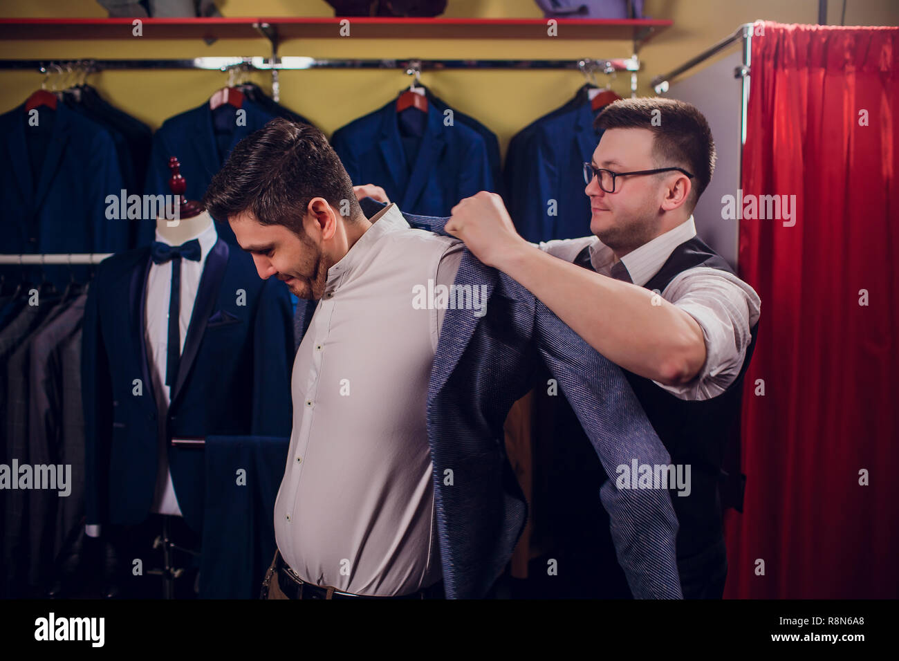 Businessman in classic vest against row suits in shop. Man helps ...