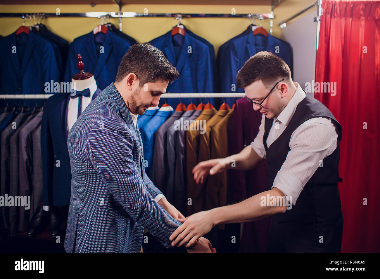 Businessman in classic vest against row suits in shop. Man helps ...