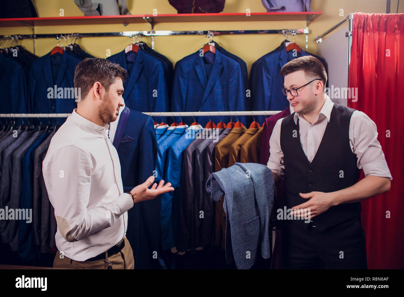 Businessman in classic vest against row suits in shop. Man helps ...