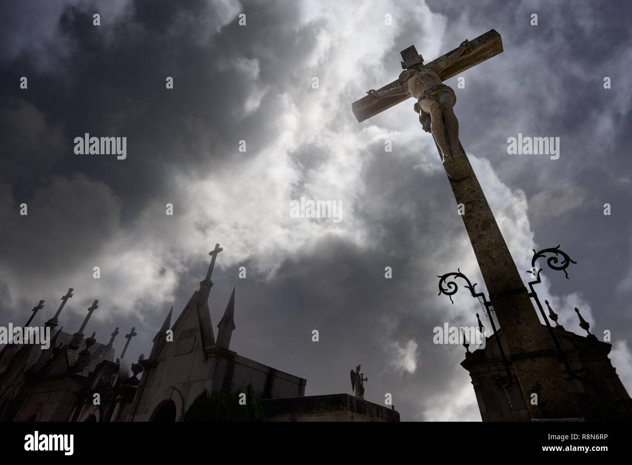 Old dark european cemetery against a dramatic cloudy sky with a crucified Christ statue on the ...