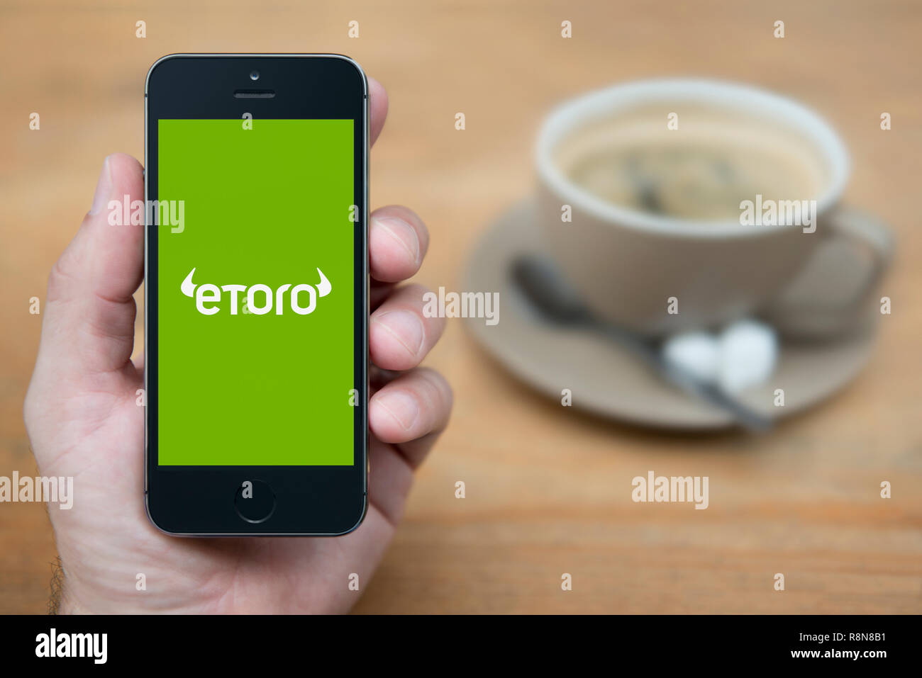 A man looks at his iPhone which displays the eToro logo (Editorial use ...