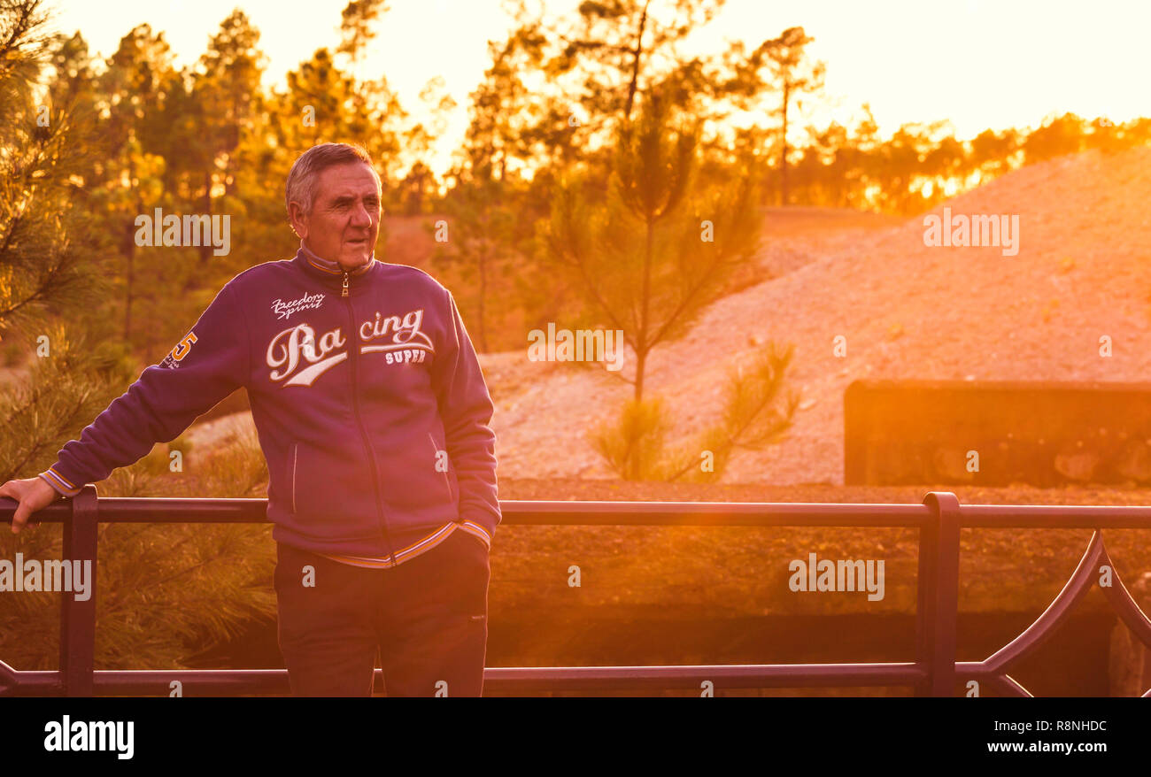 Handsome senior man posing standing leaning on handrail with sun flare ...