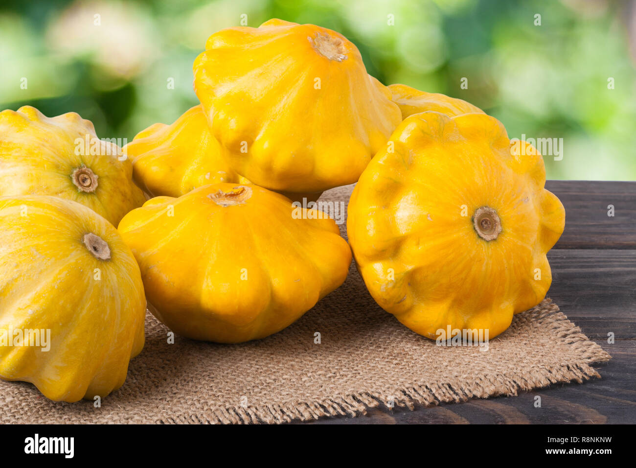 yellow squash on a wooden table with napkin of burlap and blurred green ...