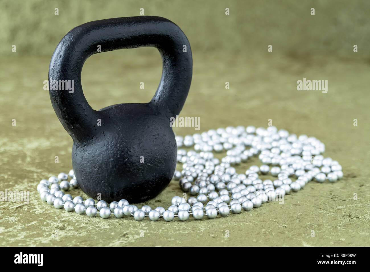 Black kettlebell on a green velvet background with silver bead garland ...