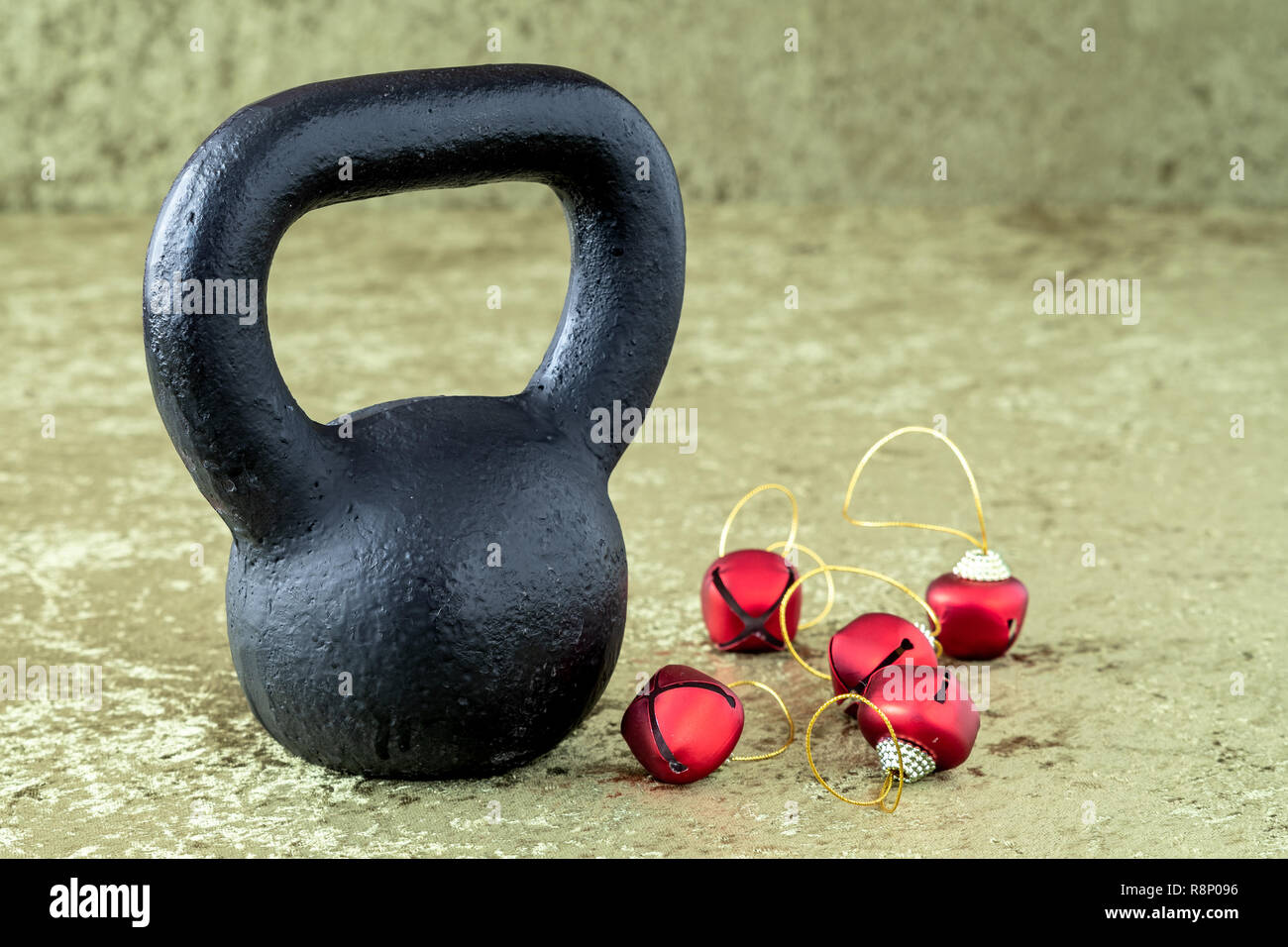 Black kettlebell on a green velvet background with red jingle bells on ...