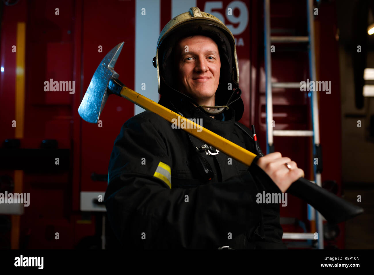 Photo of firefighter in protective helmet with hammer looking at camera ...
