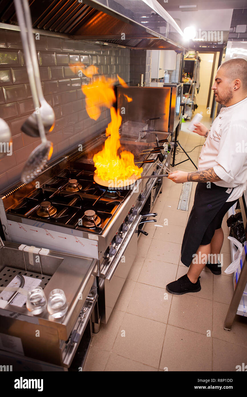 Food preparation. Chef cook in kitchen with pan over stove doing flambe ...