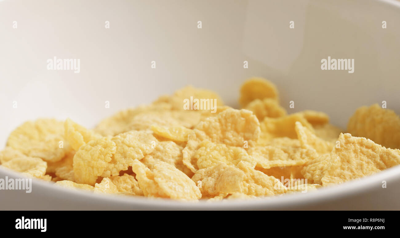 Closeup of dry corn flakes in white bowl on wood table, breakfast food ...