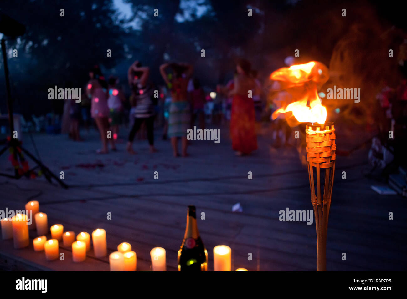 night lit torch on the beach near the water, people in the background ...