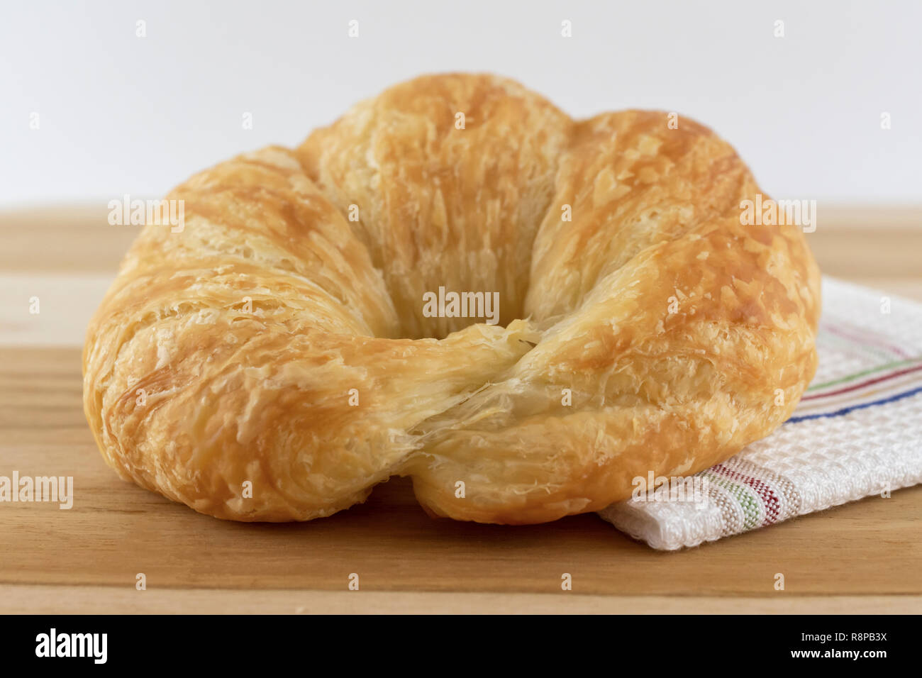 Single croissant roll on wooden cutting board with cloth. Side view ...