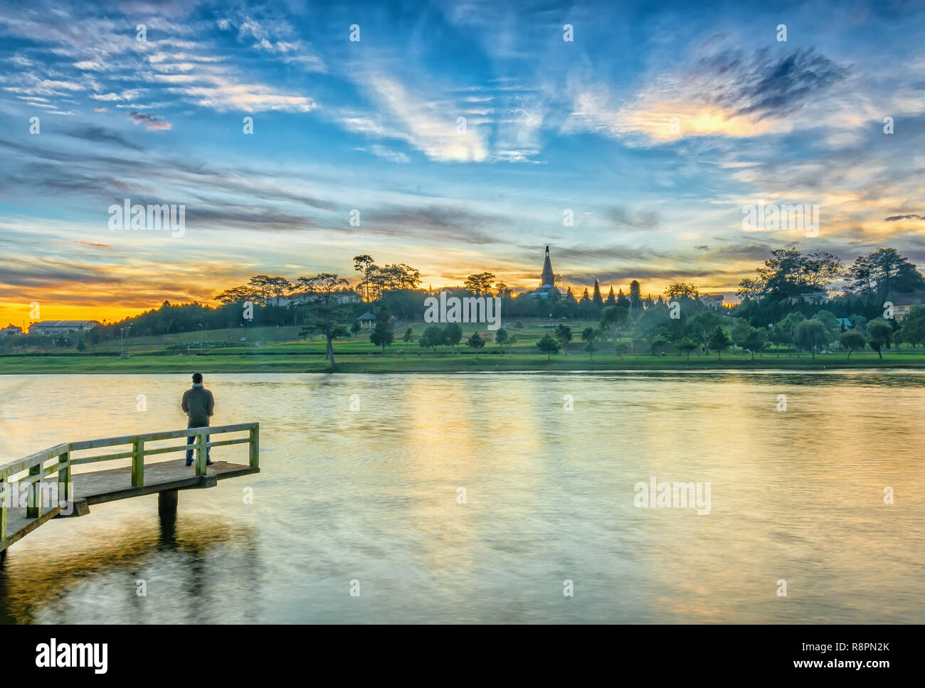 Man standing on a small bridge reflecting on the lake at sunrise as a ...
