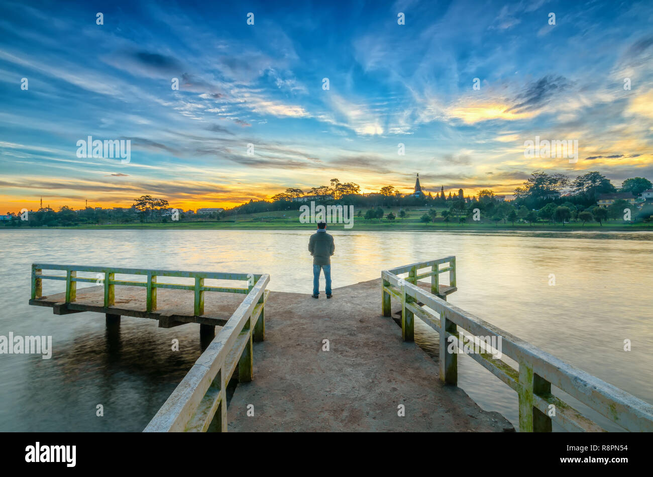Man standing on a small bridge reflecting on the lake at sunrise as a ...