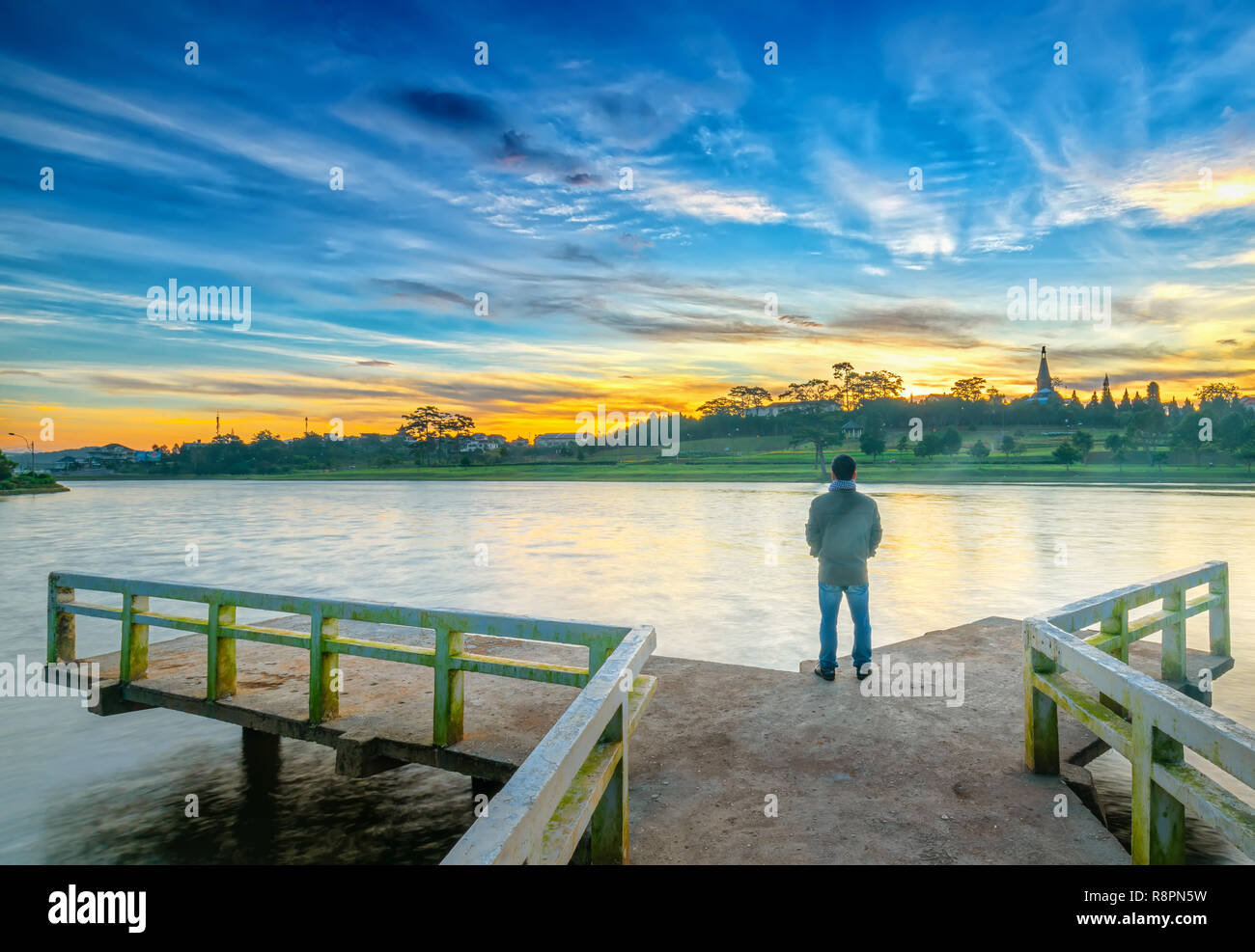 Man standing on a small bridge reflecting on the lake at sunrise as a ...