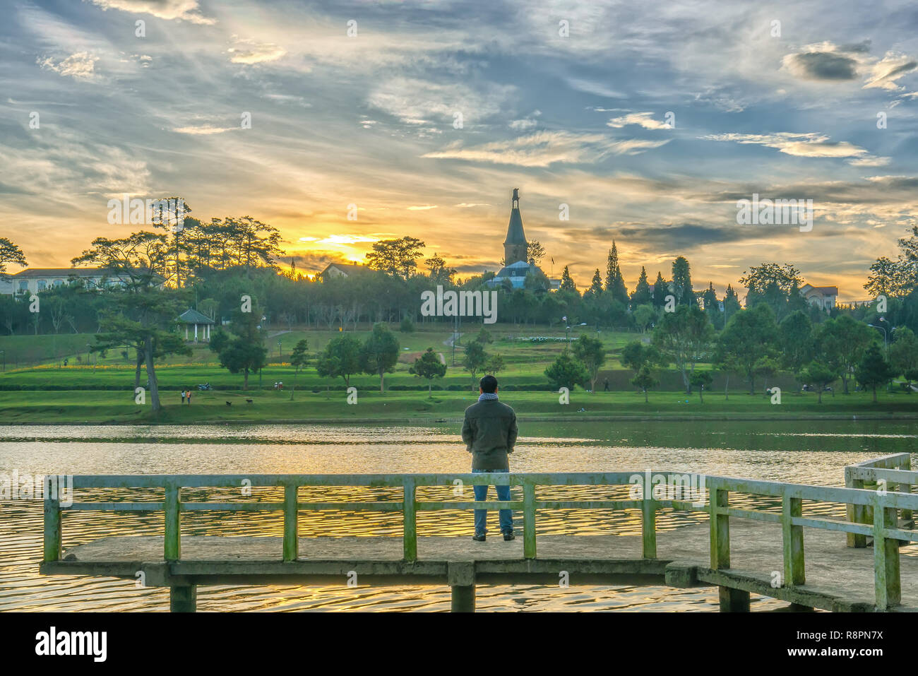 Man standing on a small bridge reflecting on the lake at sunrise as a ...